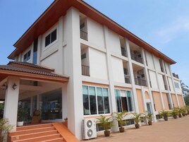 Um hotel com vários andares, fachada branca, varandas e entrada coberta com degraus.