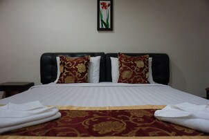Cama bem arrumada com colcha estampada em vermelho e dourado, duas almofadas brancas e um quadro com moldura vermelha e verde na parede.