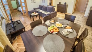 Uma área de refeições com mesa de madeira posta para o café da manhã, com pratos de frutas e doces.