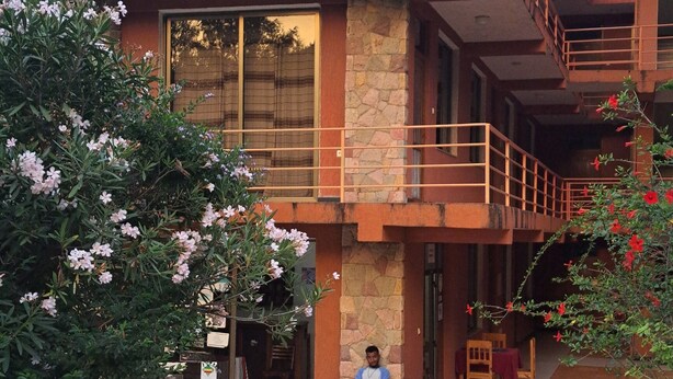 Um edifício moderno com fachada de pedra, uma área de estar coberta ao ar livre e uma pessoa sentada num banco.