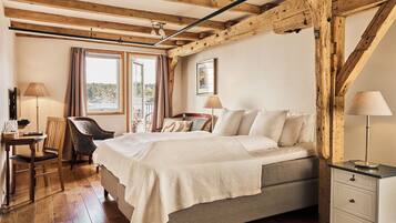 Quarto com cama, mesas de cabeceira, uma cadeira, escrivaninha e janela com cortinas.