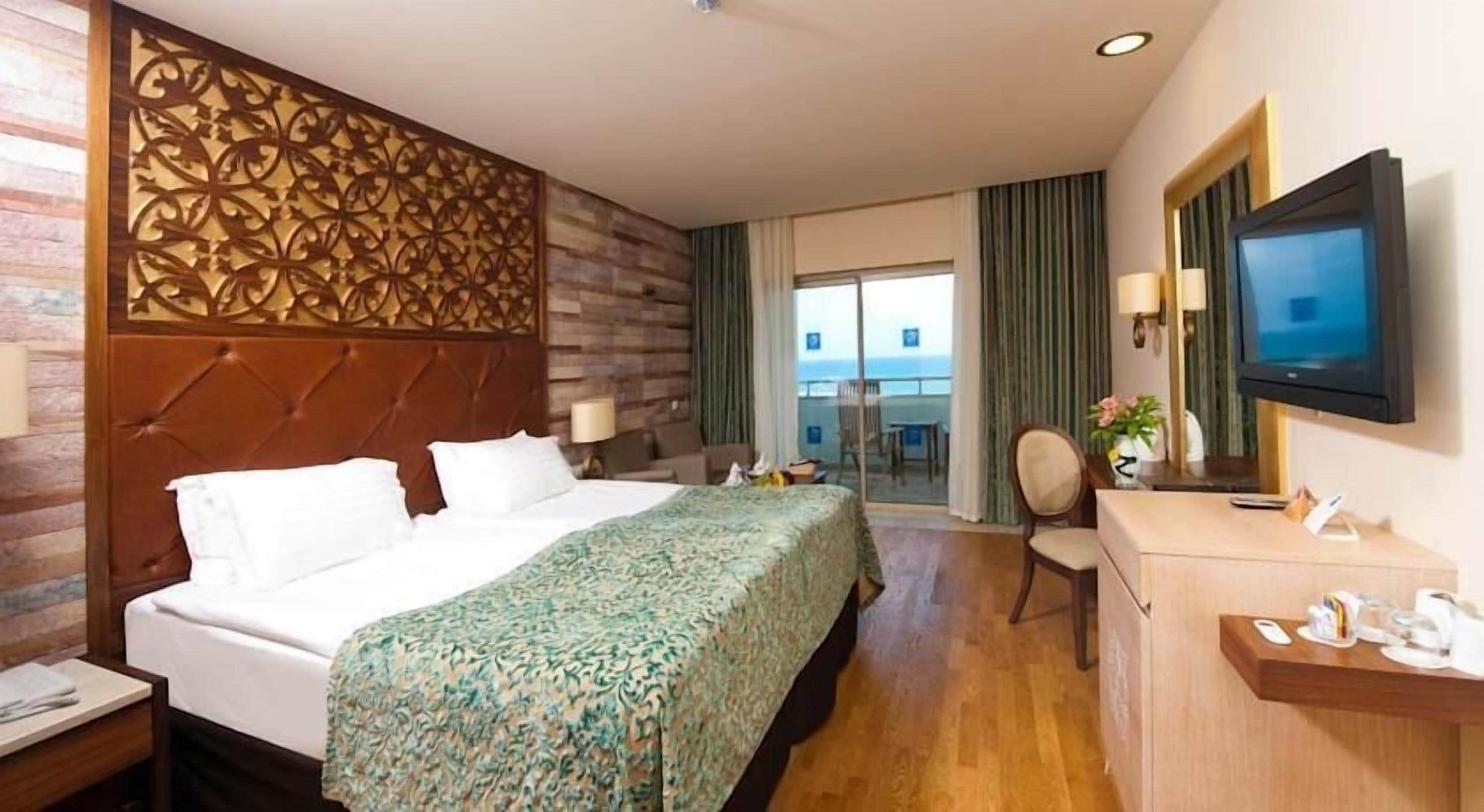 Quarto de hotel com cama grande, escrivaninha com televisão e vista para o exterior.