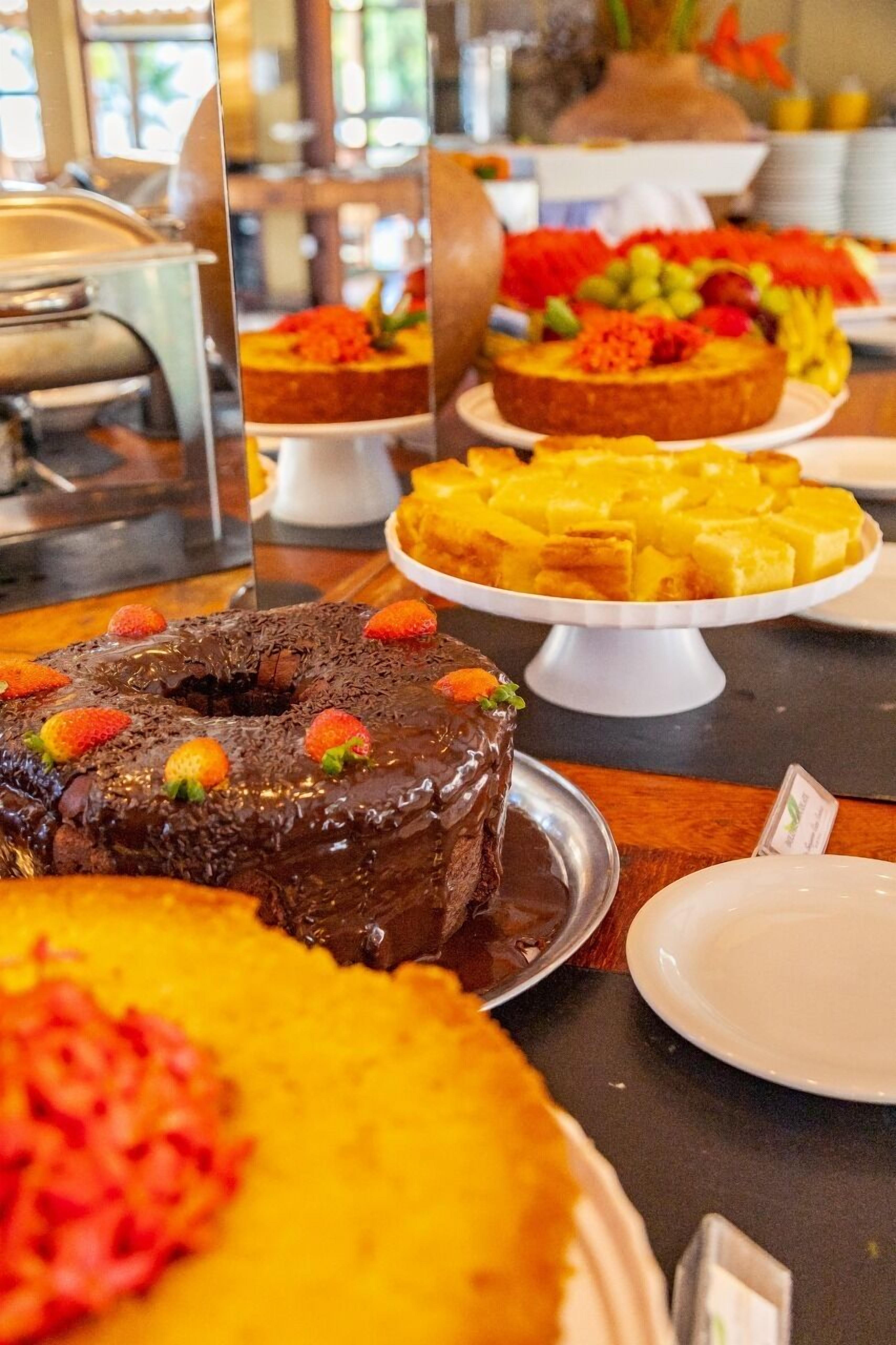 Um buffet com diversos doces, incluindo um bolo de chocolate, um bolo amarelo e uma salada de frutas.