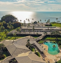 Um resort com piscina, palmeiras e vista para o oceano.
