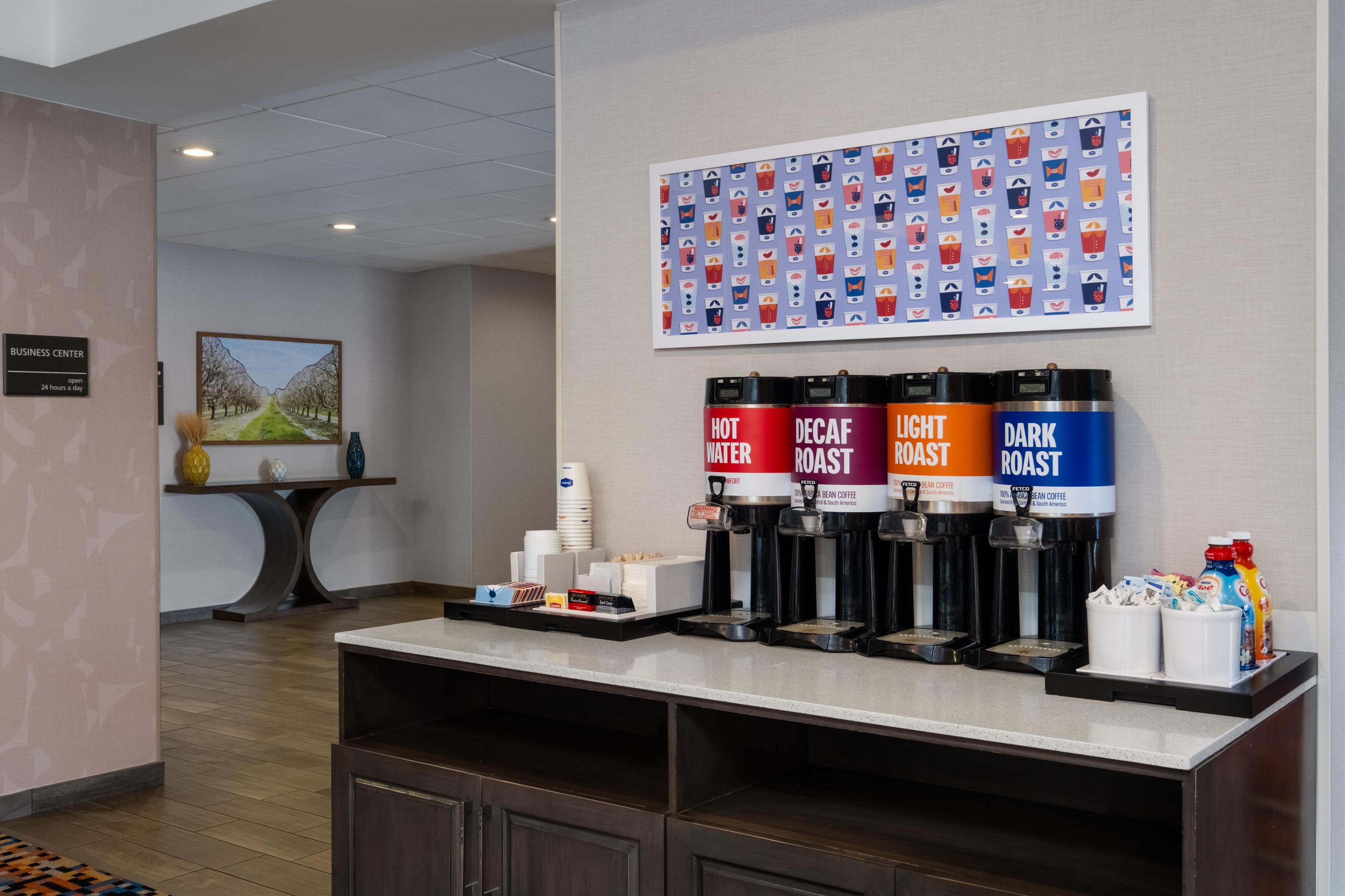 Estação de café com quatro dispensadores identificados como água quente, descafeinado, torra clara e torra escura.
