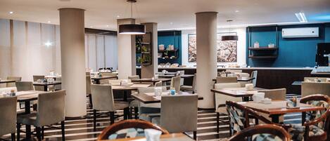 Um restaurante moderno com mesas e cadeiras altas, chão riscado e uma parede azul como detalhe.