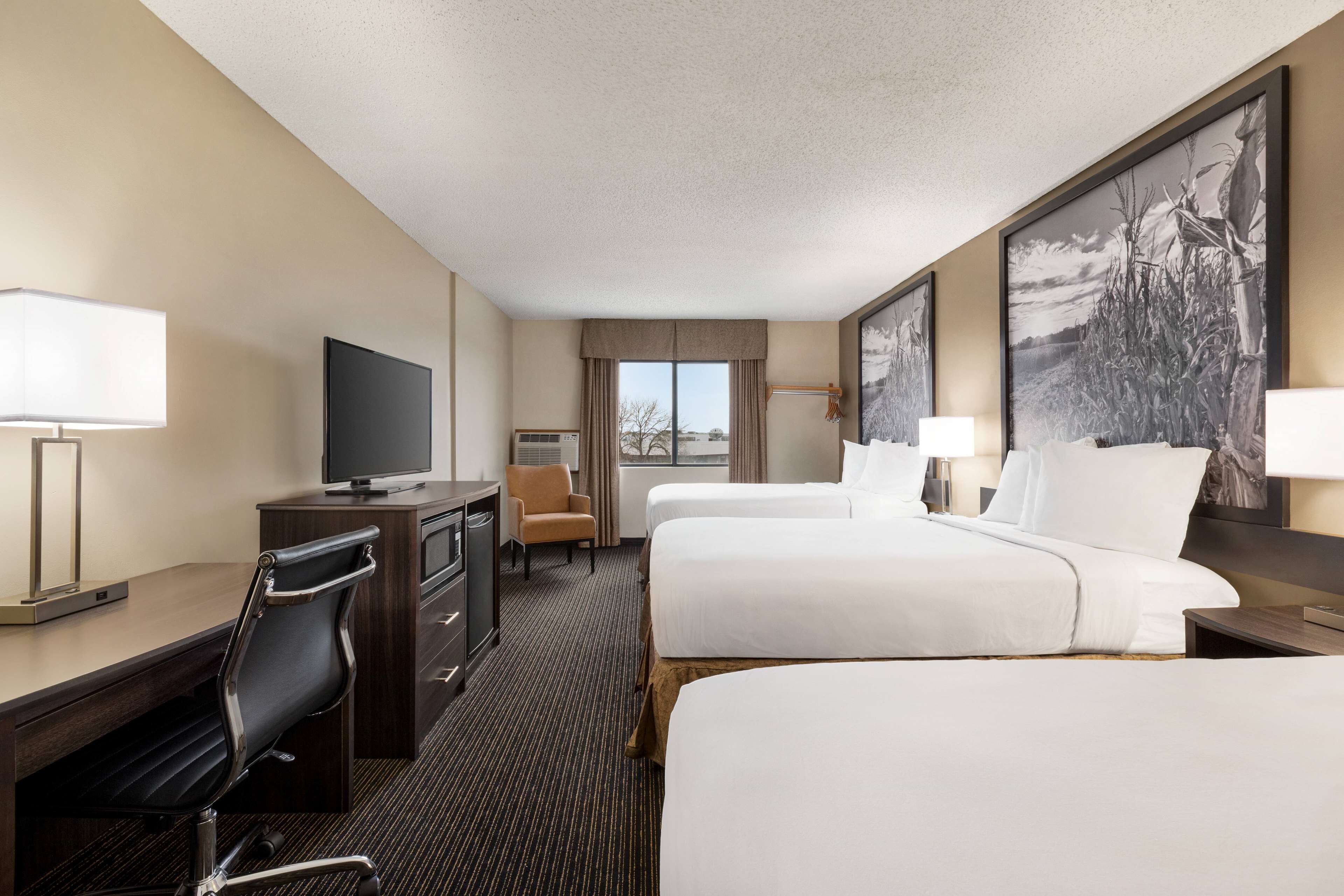 Quarto de hotel com duas camas, uma escrivaninha com cadeira, televisão e uma janela grande.