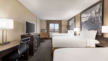 Quarto de hotel com duas camas, uma escrivaninha com cadeira, televisão e uma janela grande.