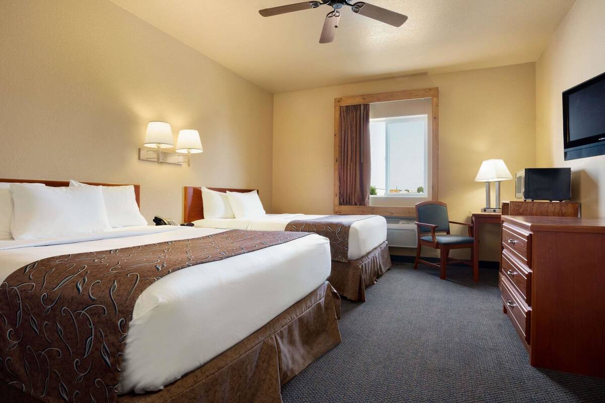 Quarto de hotel com duas camas, uma escrivaninha, uma cadeira, uma televisão e um espelho.