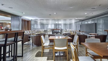 Uma sala de jantar espaçosa com várias mesas e cadeiras, piso de madeira polida e design de teto moderno.