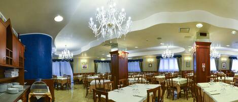Uma ampla sala de jantar com várias mesas e cadeiras, um lustre e uma parede azul decorativa.