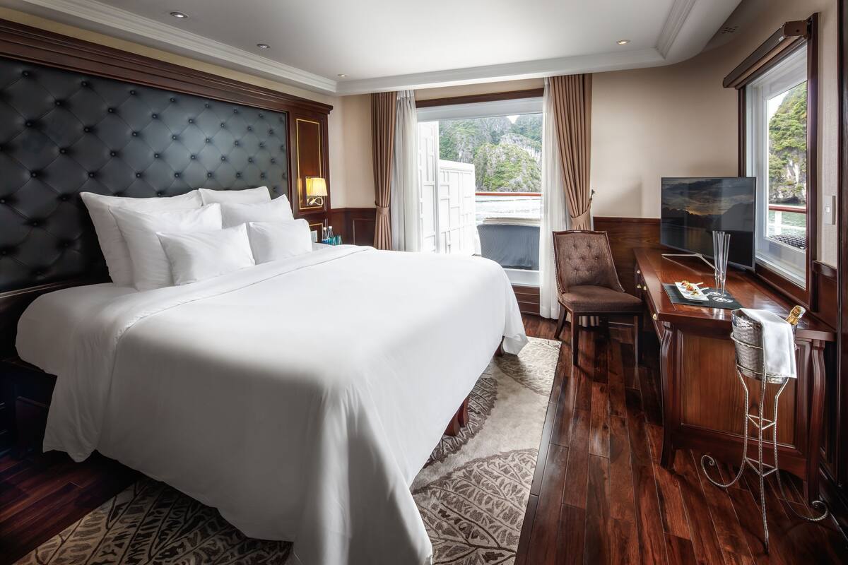 Quarto de hotel com uma cama grande, uma mesa de trabalho com uma televisão e vista para o exterior.