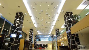 Um hall de hotel moderno com teto alto, decorações esféricas refletoras e uma área de recepção com painel digital.