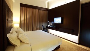 Quarto de hotel com uma cama grande, uma escrivaninha com computador, televisão e cortina.