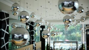 Um interior moderno com espelhos esféricos pendurados no teto, padrões geométricos nas paredes e vista do exterior através de grandes janelas.