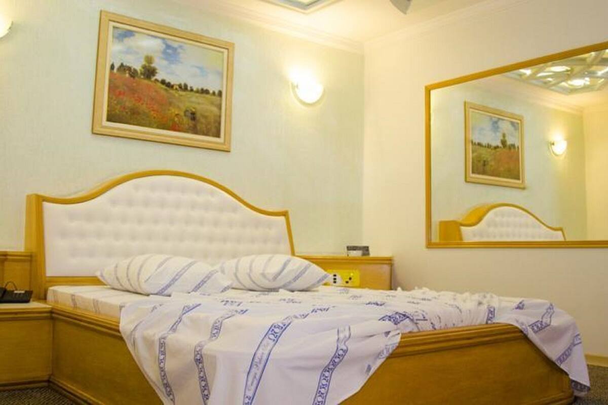 Quarto de hotel com cama, mesa de cabeceira, espelho fixado na parede e um quadro na parede.