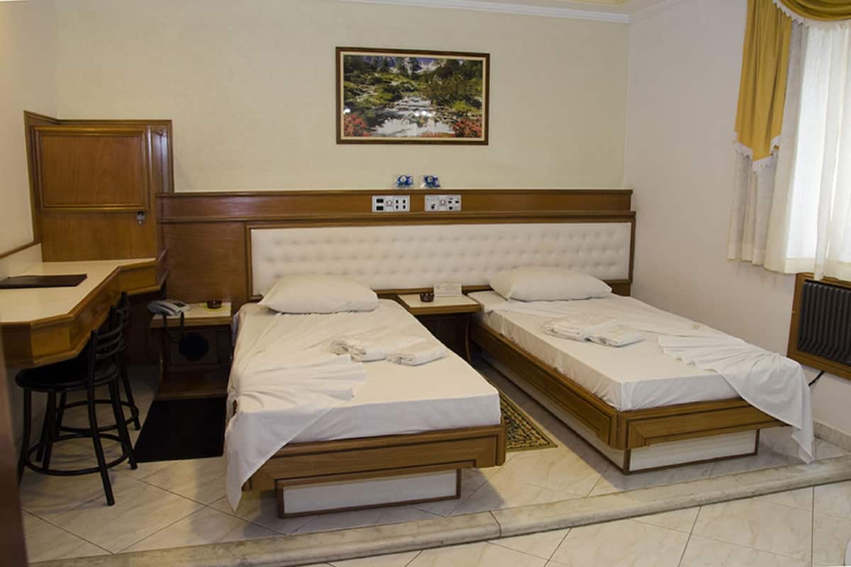 Quarto de hotel com duas camas de solteiro, uma escrivaninha e uma cadeira.