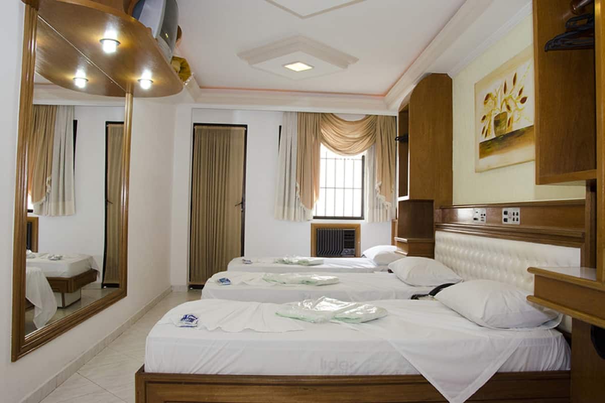Quarto de hotel com duas camas, um espelho grande, um quadro e uma janela com cortinas.