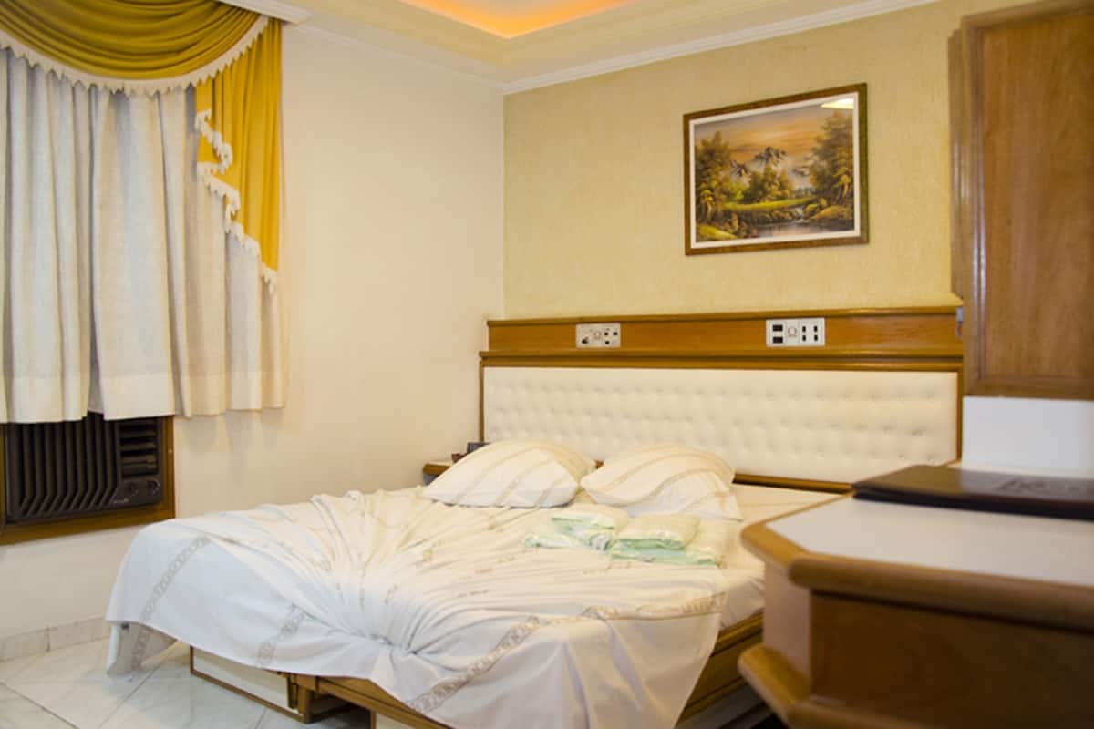 Quarto de hotel com uma cama, um quadro na parede e uma janela com cortinas.