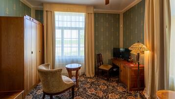 Quarto com guarda-roupa de madeira, escrivaninha com luminária, cadeira e televisão.