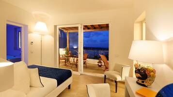 Quarto de hotel com cama, sofá, mesa com luminária e varanda com mesa e cadeiras.