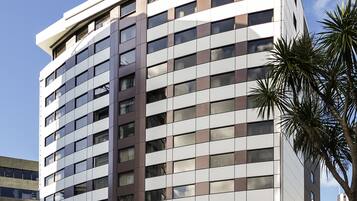 Um hotel moderno com um logotipo visível no topo, vários andares com grandes janelas e uma placa na base indicando o nome.