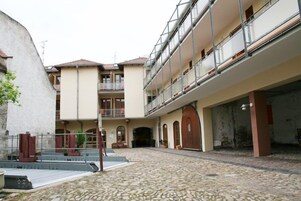 Um pátio com piso de laje, uma escadaria central e um edifício com várias varandas e portas em arco.
