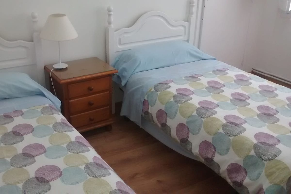Quarto com duas camas, uma mesa de cabeceira e uma luminária.