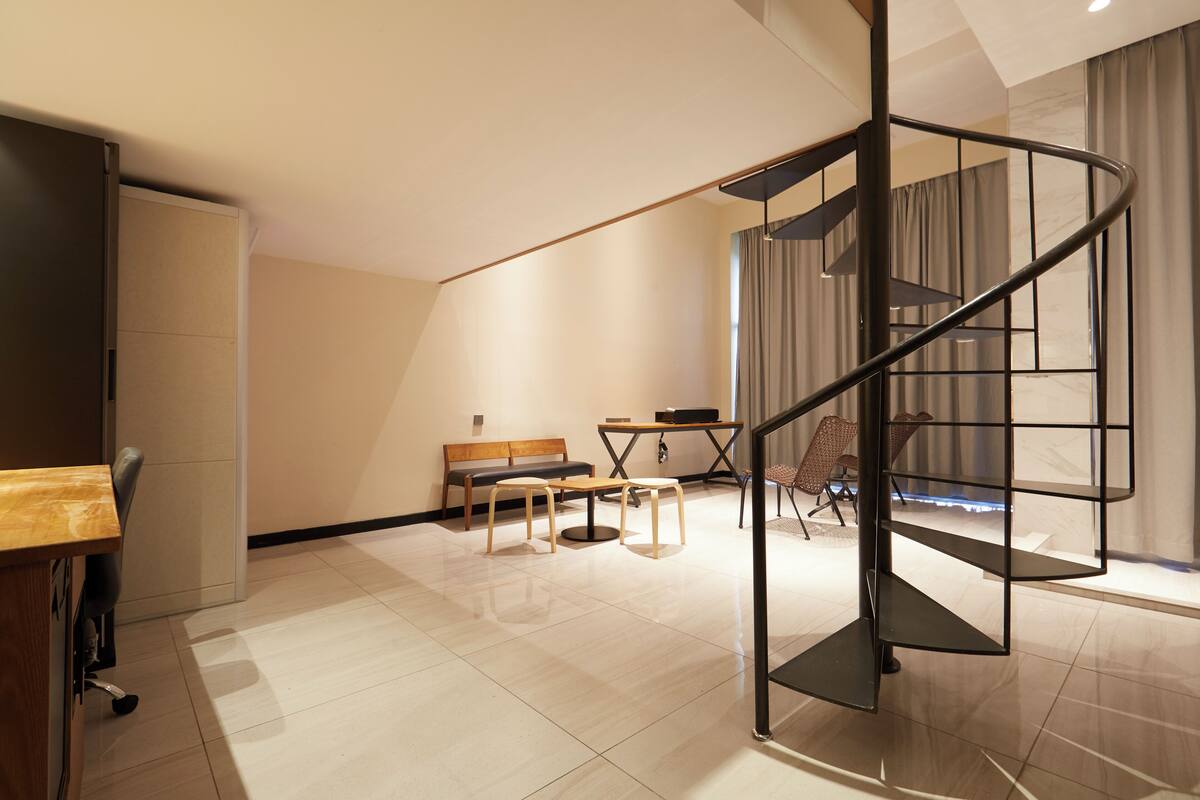 Um interior moderno com uma escrivaninha de madeira, um banco, uma pequena mesa e uma escada em espiral.