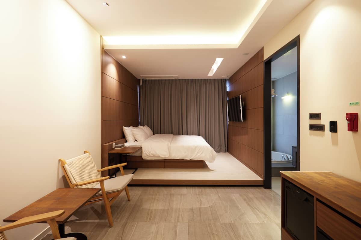 Quarto de hotel moderno com cama, escrivaninha, cadeira e televisão.