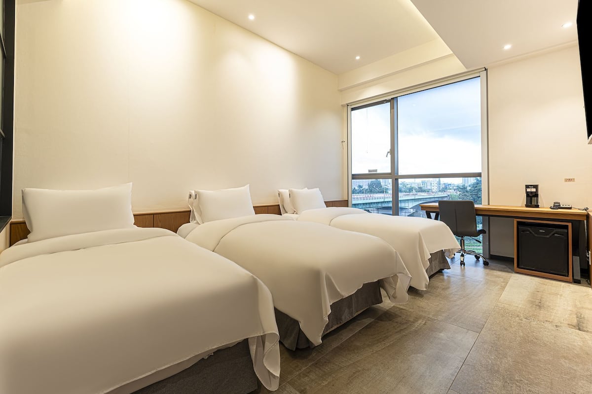 Quarto de hotel com três camas, uma escrivaninha e vista para a cidade.