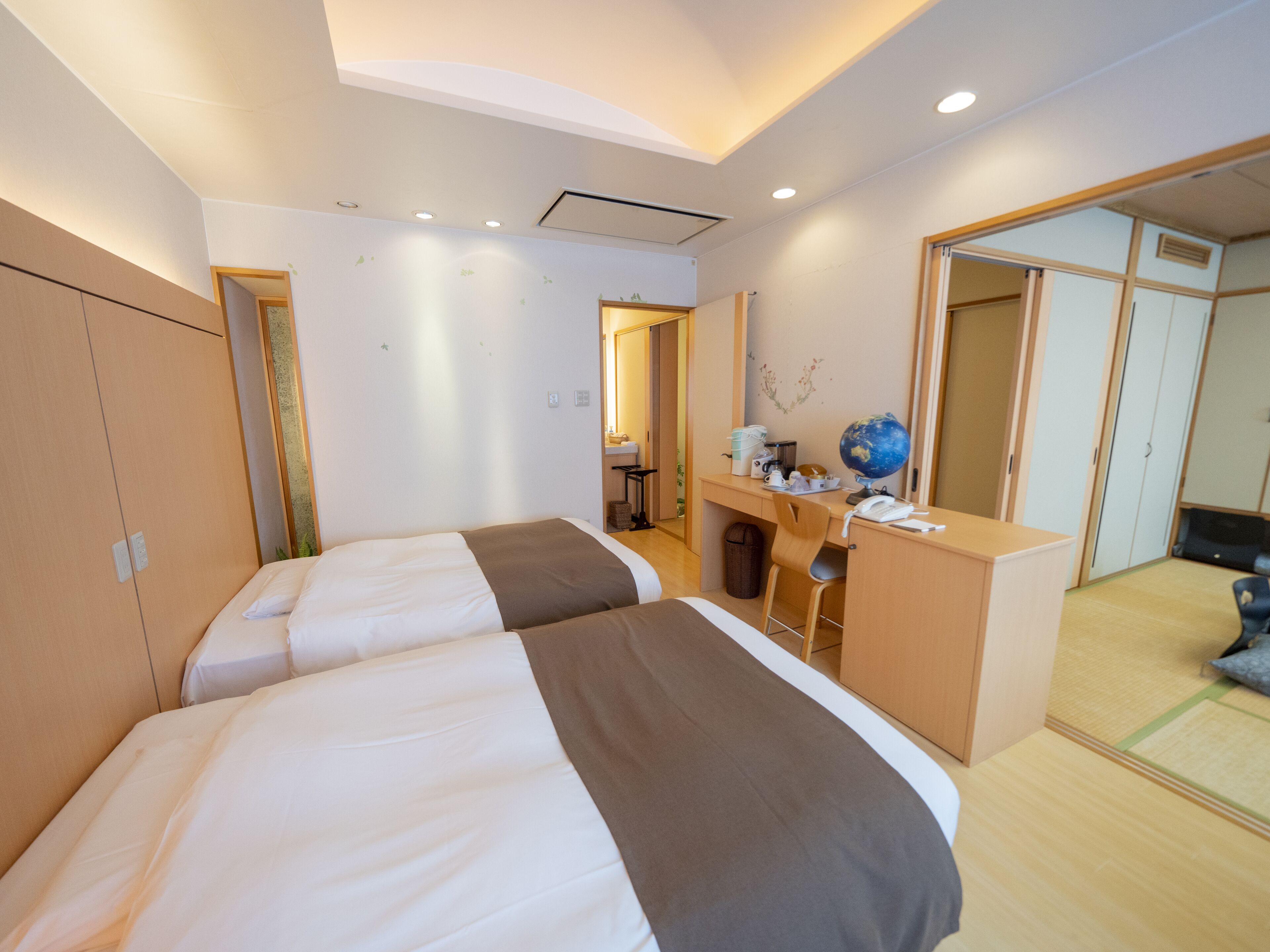 Quarto de hotel com duas camas, uma escrivaninha, um globo e um guarda-roupa.
