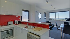 Uma cozinha moderna com armários brancos, painel de fundo vermelho, forno embutido e lava-louças.