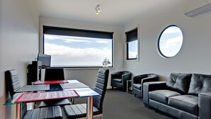 Quarto de hotel moderno com uma janela grande, um espelho redondo, um sofá de couro e uma mesa de jantar de vidro com cadeiras.