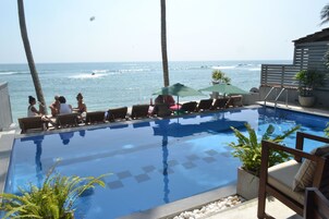 Área da piscina com espreguiçadeiras e guarda-sóis, com vista para o oceano.