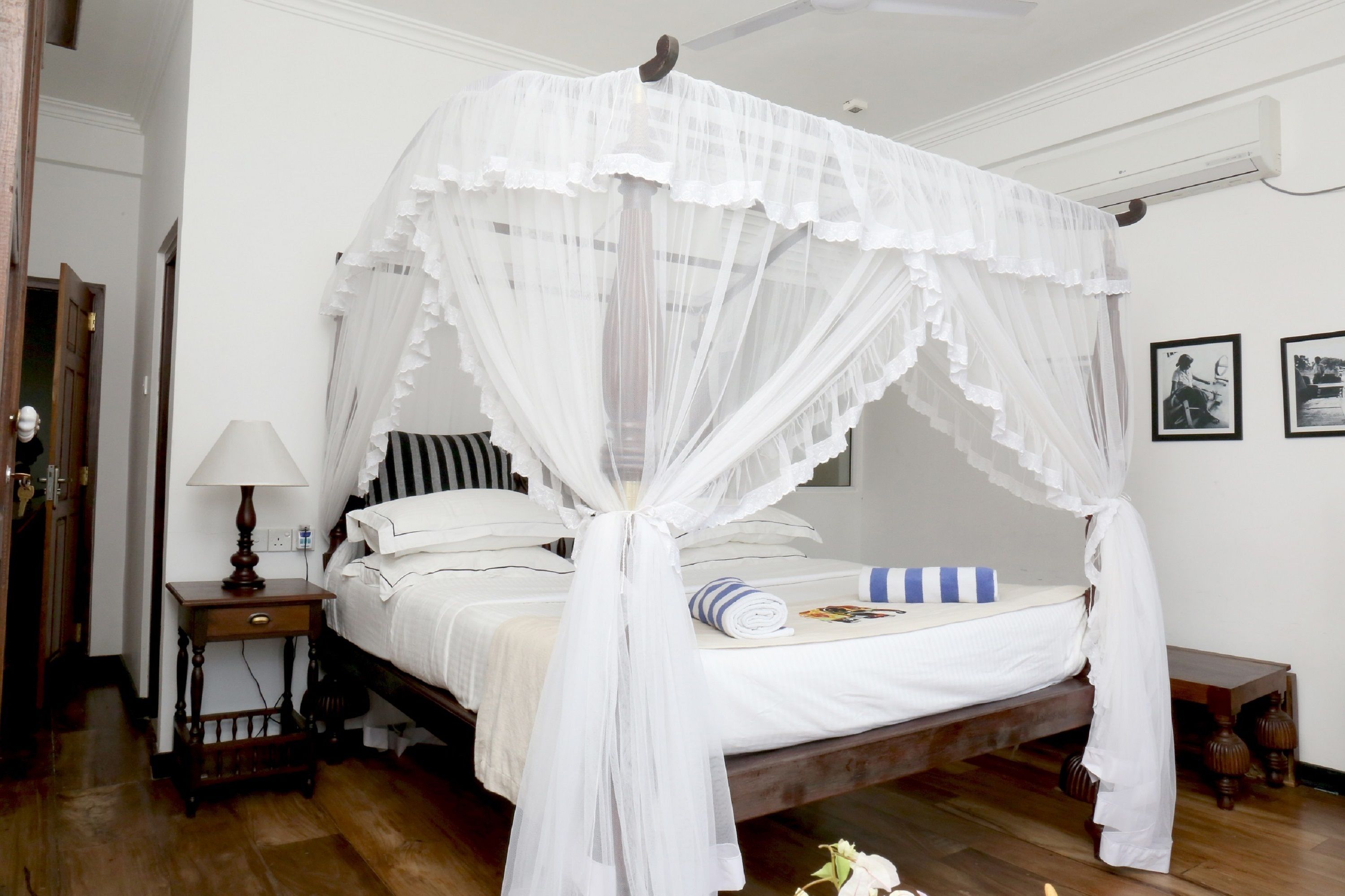 Um quarto com uma cama de dossel, uma mesa de cabeceira com luminária e um criado-mudo de madeira.