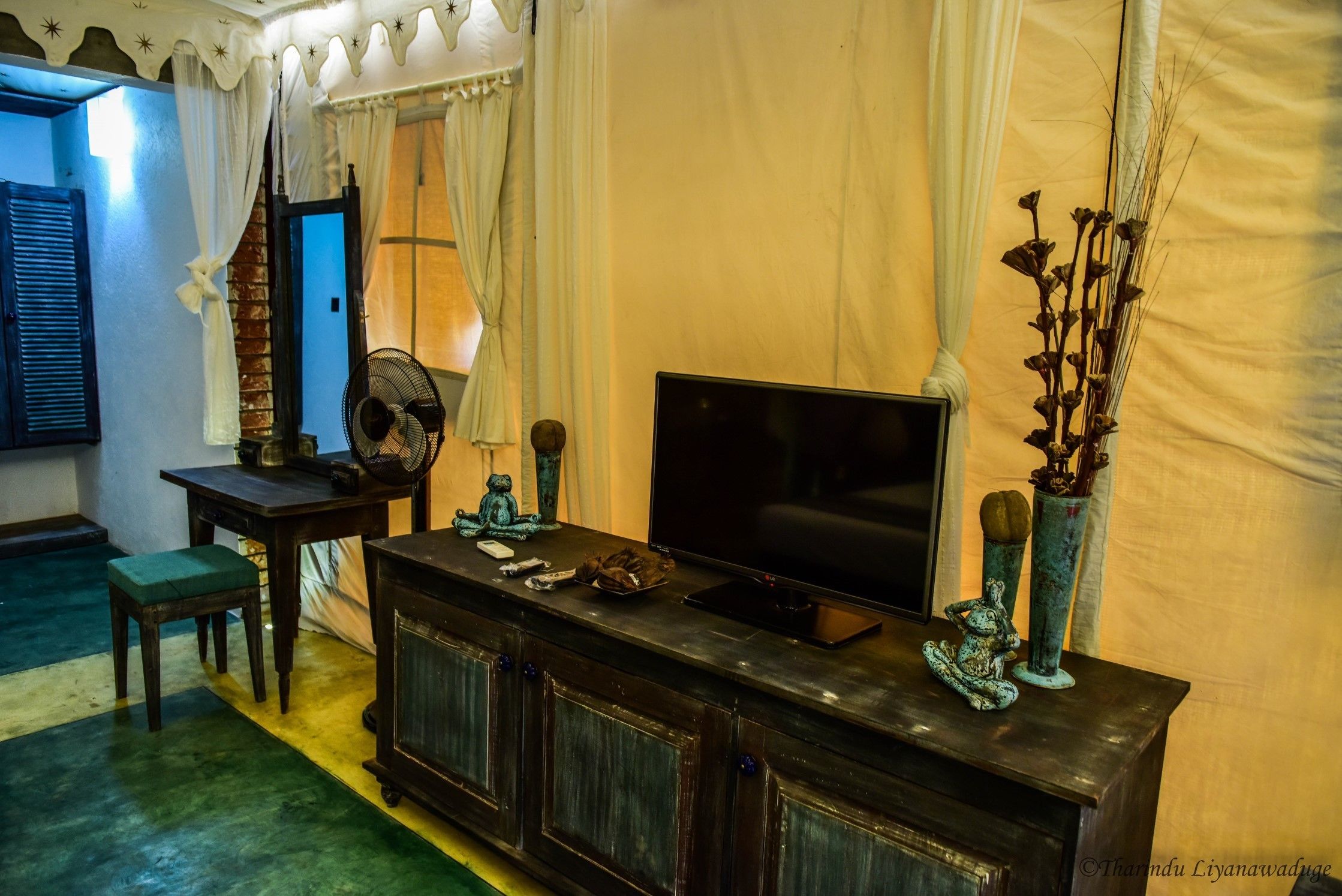 Sala de estar com televisão sobre um armário de madeira, uma mesinha com um ventilador e objetos decorativos.