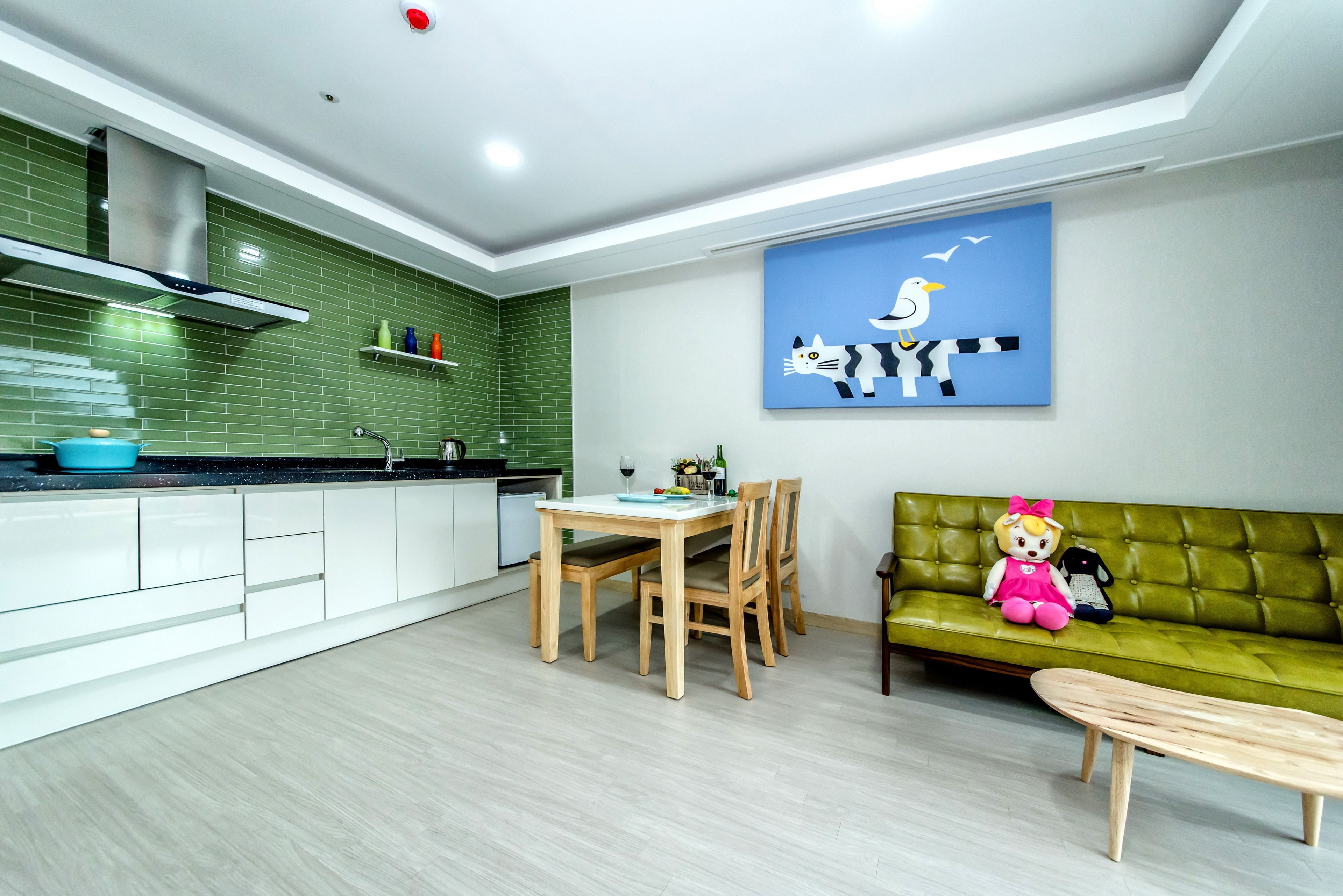 Uma cozinha moderna com armários brancos, painel de fundo verde e um espaço de refeições com mesa e cadeiras.