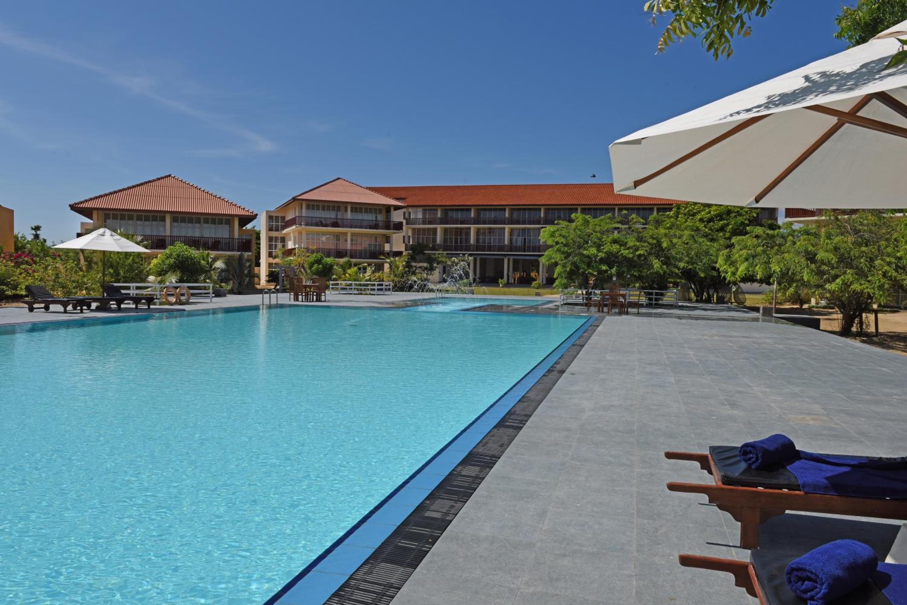 Piscina com espreguiçadeiras e guarda-sóis, cercada por edifícios com telhados vermelhos.