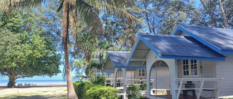 Uma propriedade à beira-mar com duas cabanas brancas e telhados azuis, rodeada por vegetação exuberante e palmeiras.