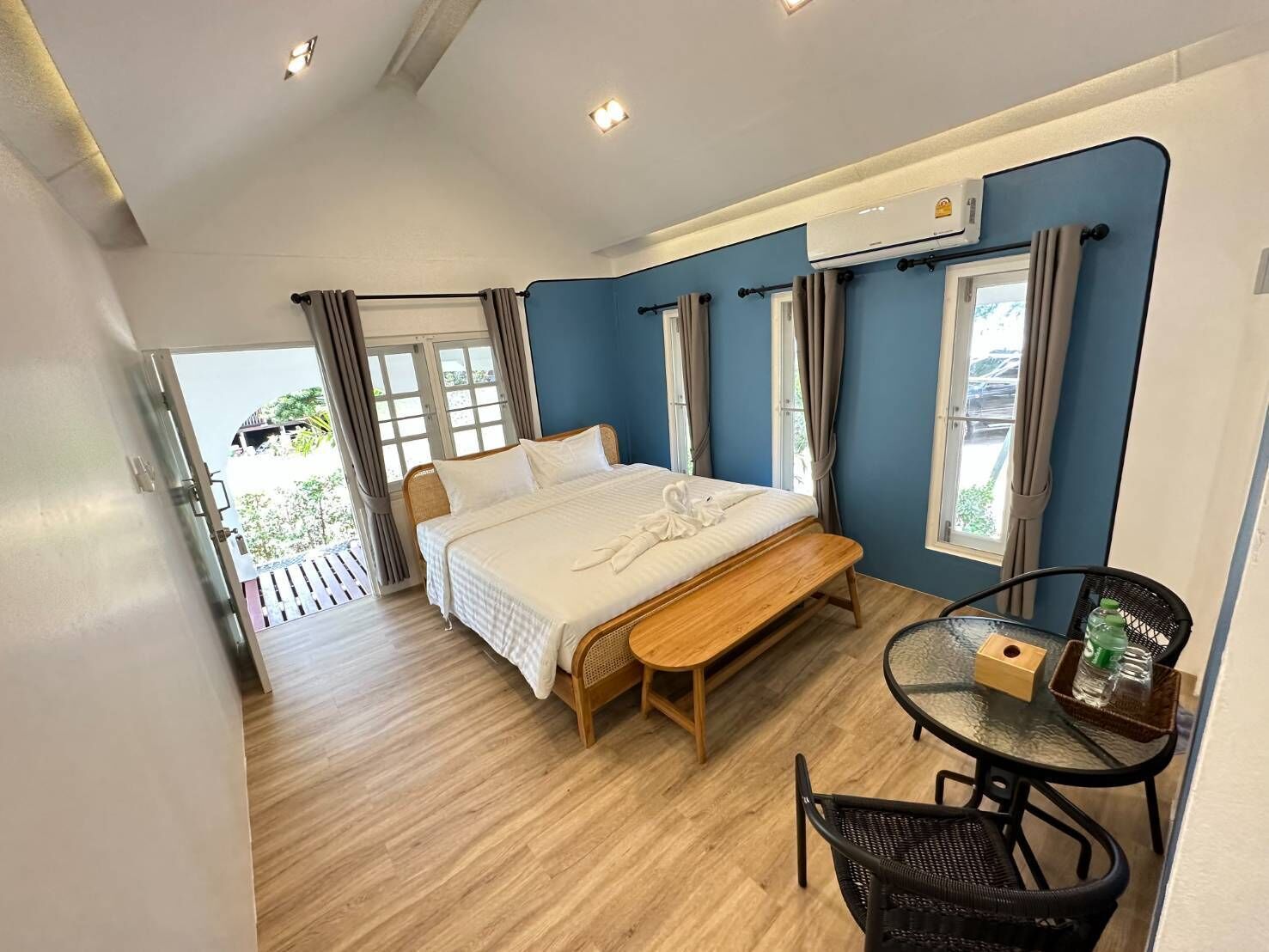 Quarto de hotel com cama, uma mesinha, uma cadeira e uma janela com cortinas.