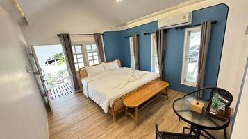 Quarto de hotel com cama, uma mesinha, uma cadeira e uma janela com cortinas.