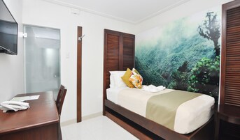 Quarto de hotel com uma cama, uma escrivaninha, uma cadeira, uma televisão e um mural grande com tema de floresta na parede.