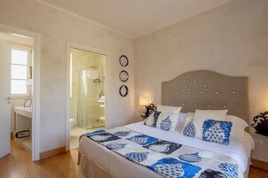Quarto com cama grande, mesa de cabeceira e relógio fixado na parede.