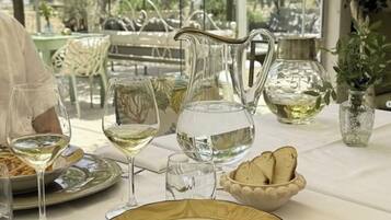 Uma mesa posta para refeição, com um prato de massa, copos de vinho e um jarro de água.