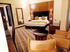Quarto de hotel com uma cama grande, uma mesa de centro redonda, uma poltrona de couro e um espelho.