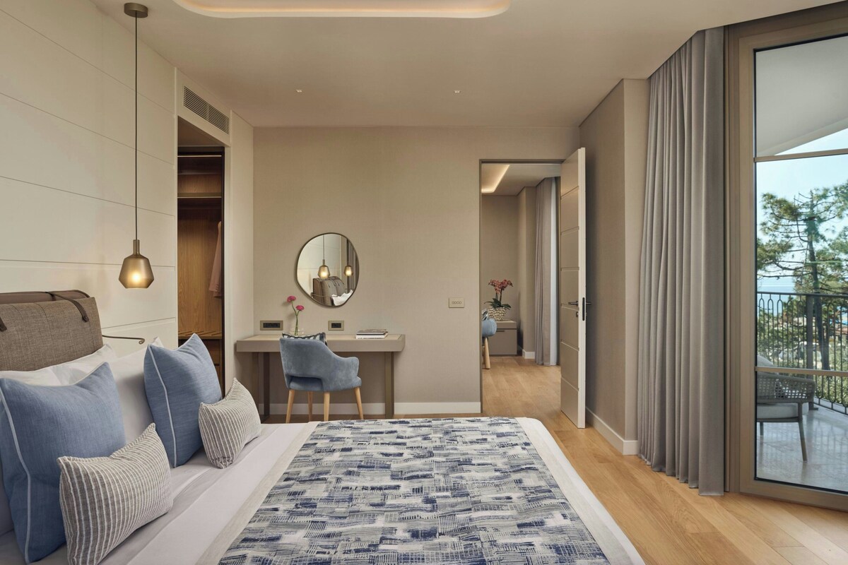 Quarto moderno com uma cama grande, uma escrivaninha, um espelho e vista para o exterior.