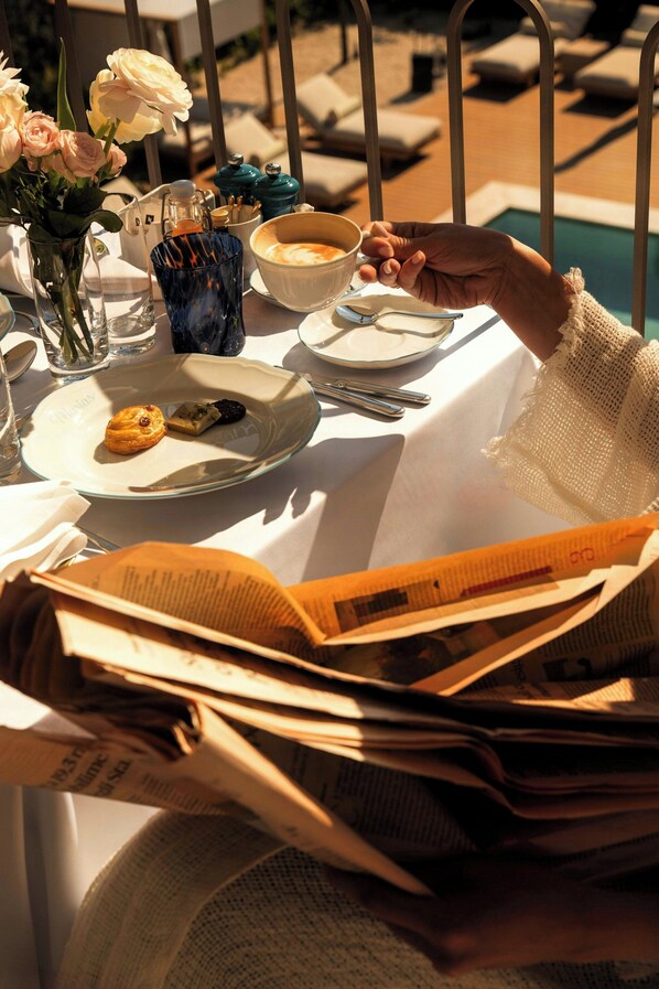 Uma mesa de jantar com um prato de comida, uma tigela, um livro e um vaso de flores.