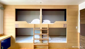 Quarto com beliche, uma escada, duas camas e uma pequena mesa.