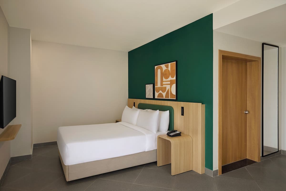 Quarto de hotel com cama, mesa de cabeceira com telefone, TV em suporte e uma parede verde de destaque.